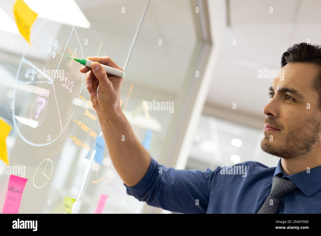 Focused caucasian man working and writing on glass board in office ...