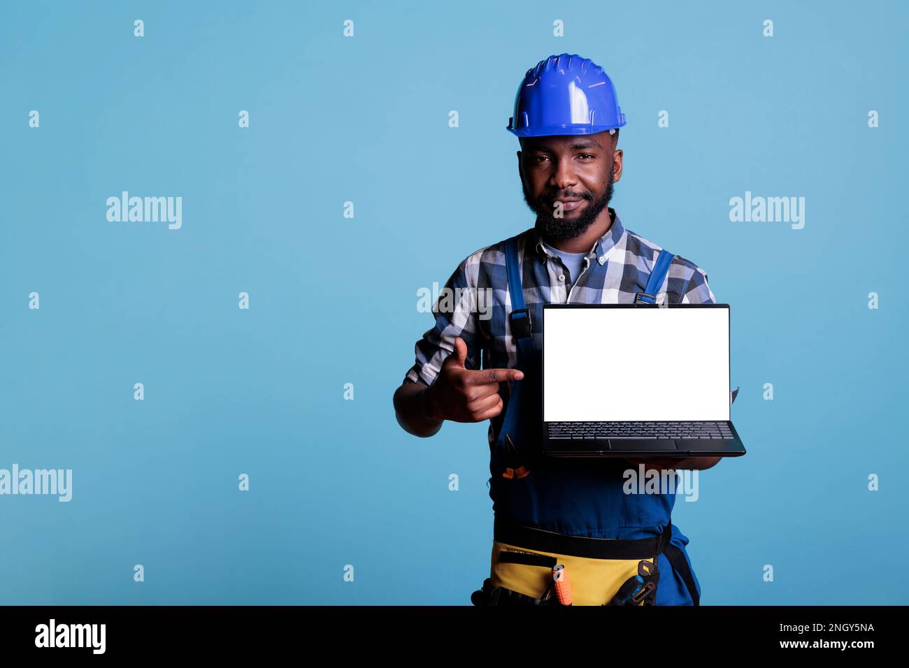 Smiling african american construction worker pointing at empty laptop screen with copy space ...