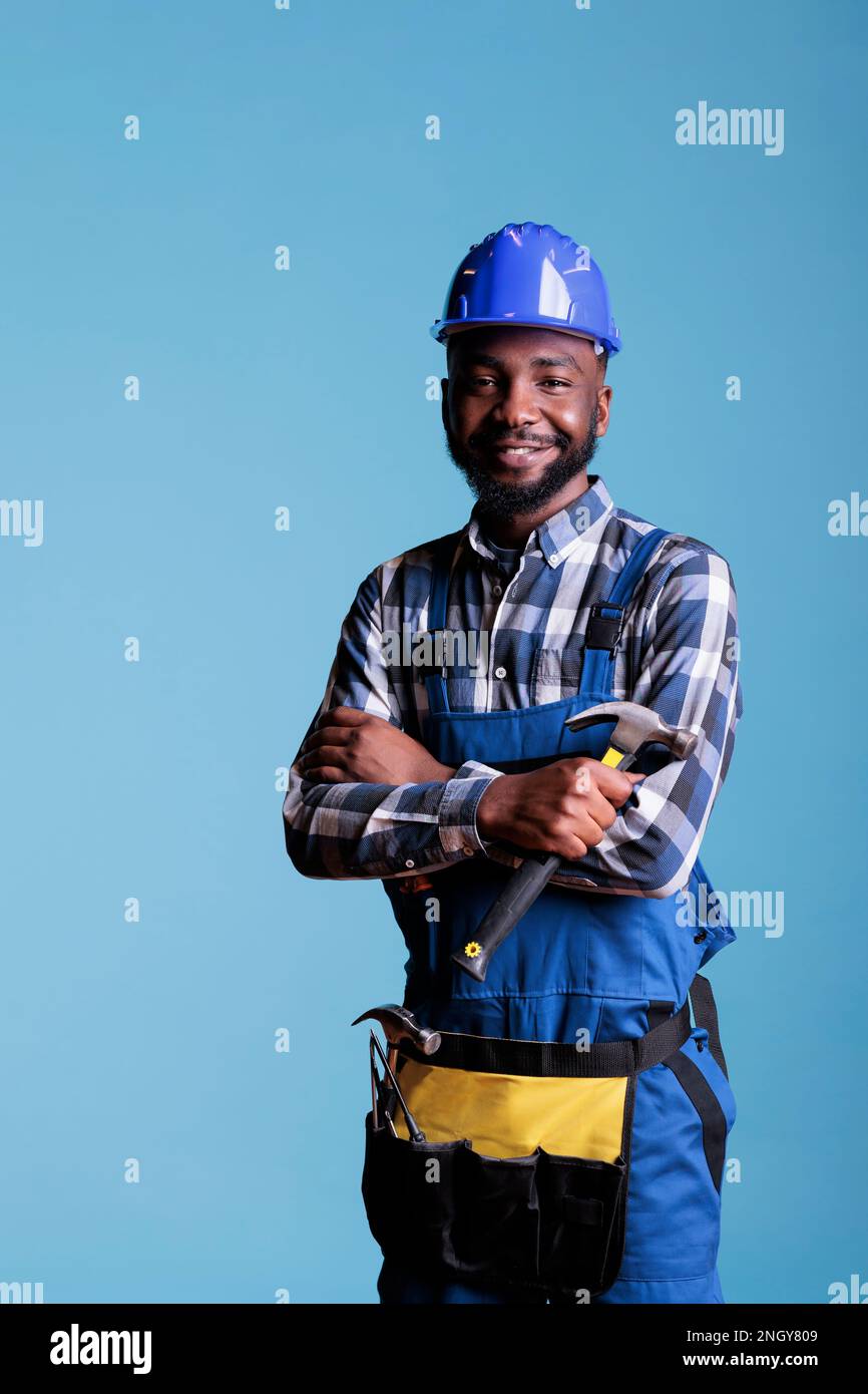 Happy African american builder holding hammer posing in studio against ...