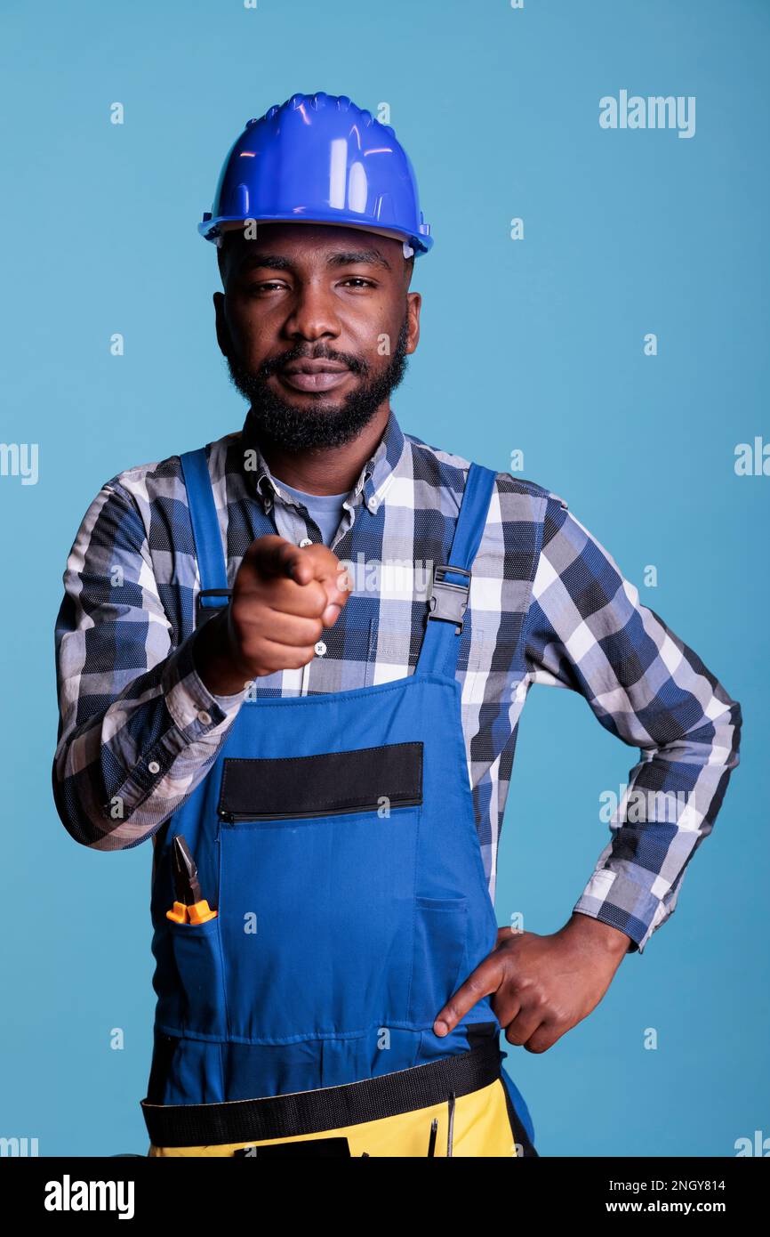 Portrait of hard hatted builder pointing at camera, looking determined ...