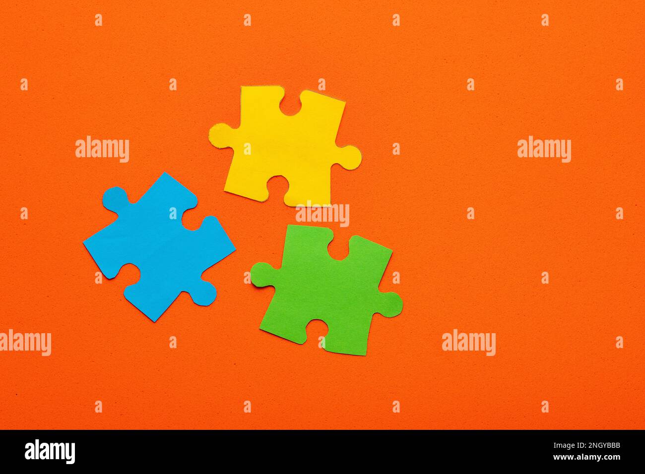 Three jigsaw puzzle pieces colored blue, green and yellow on orange ...