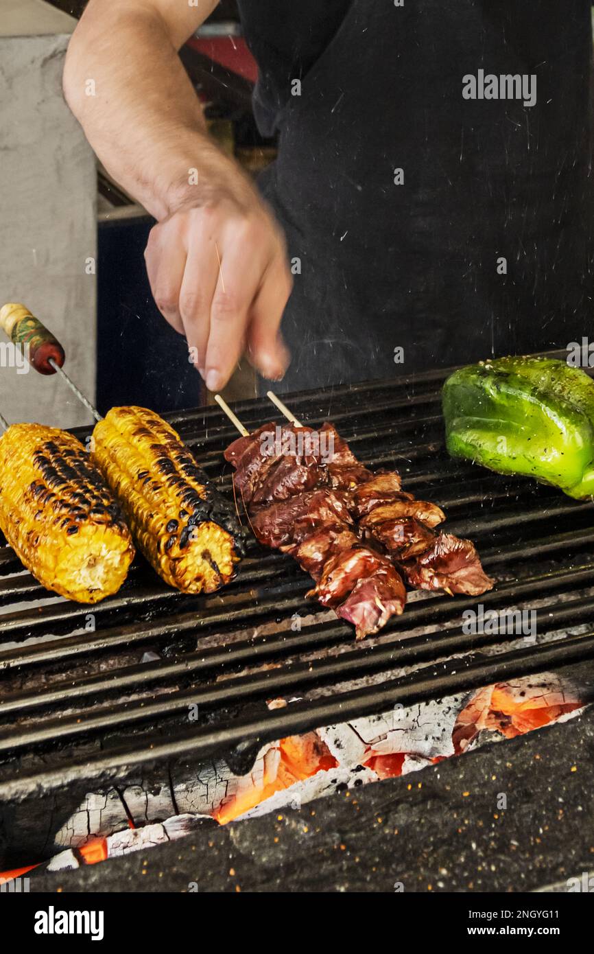 Chef flipping meat skewers, corn on the cob and green peppers over ...