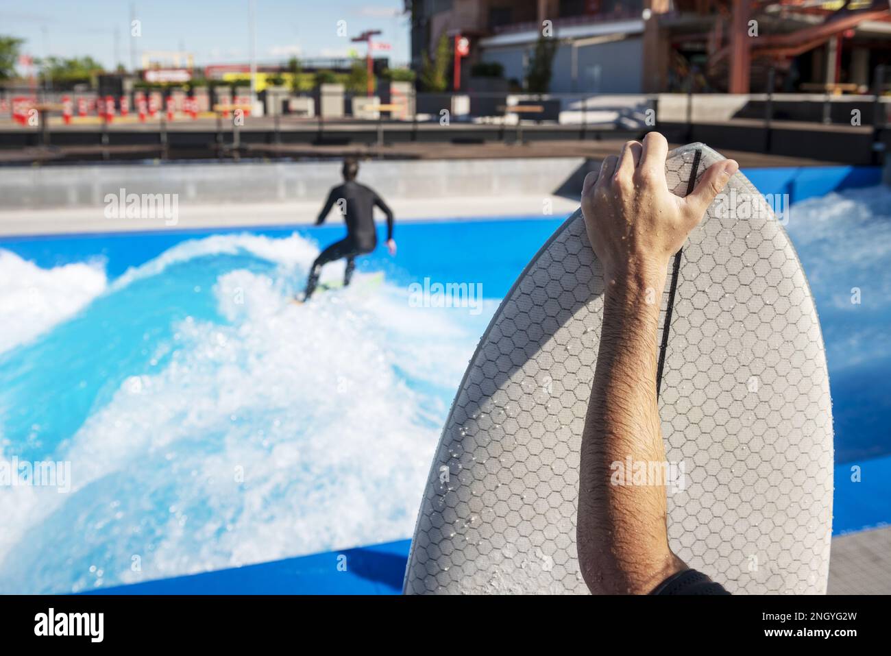 A surfer holding his wet board waiting his turn in the wave pool Stock ...