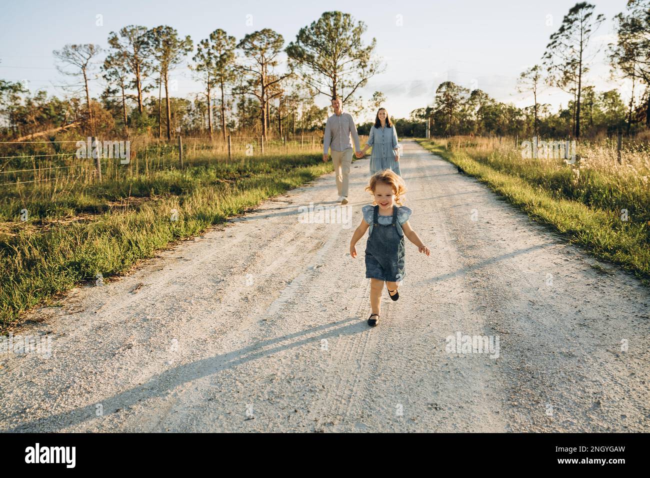 Running little girl with mom and dad behind her on the rural road Stock ...