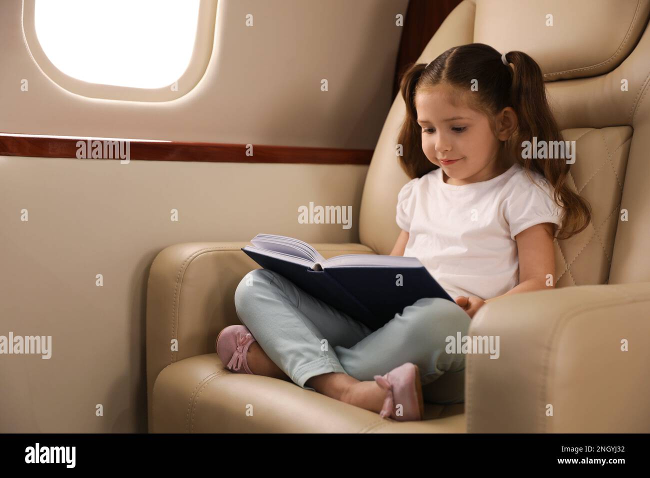 Cute little girl reading book in airplane during flight Stock Photo - Alamy