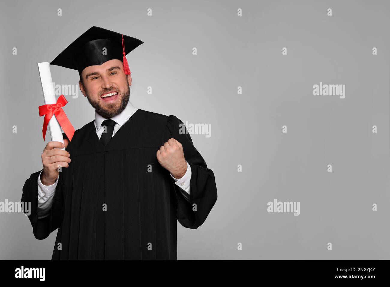 Emotional student with graduation hat and diploma on grey background ...