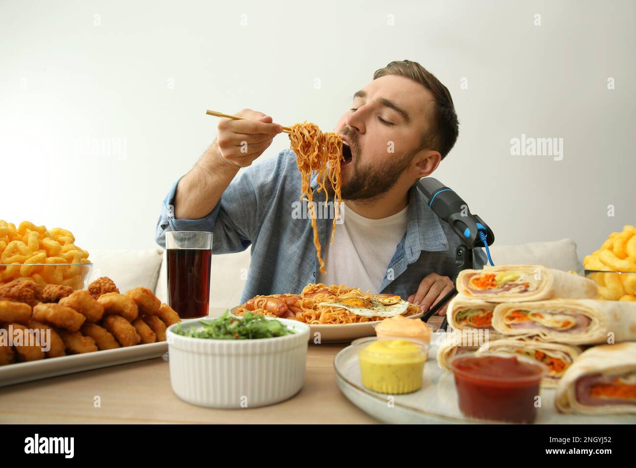 Food blogger eating in front of microphone at table against light ...