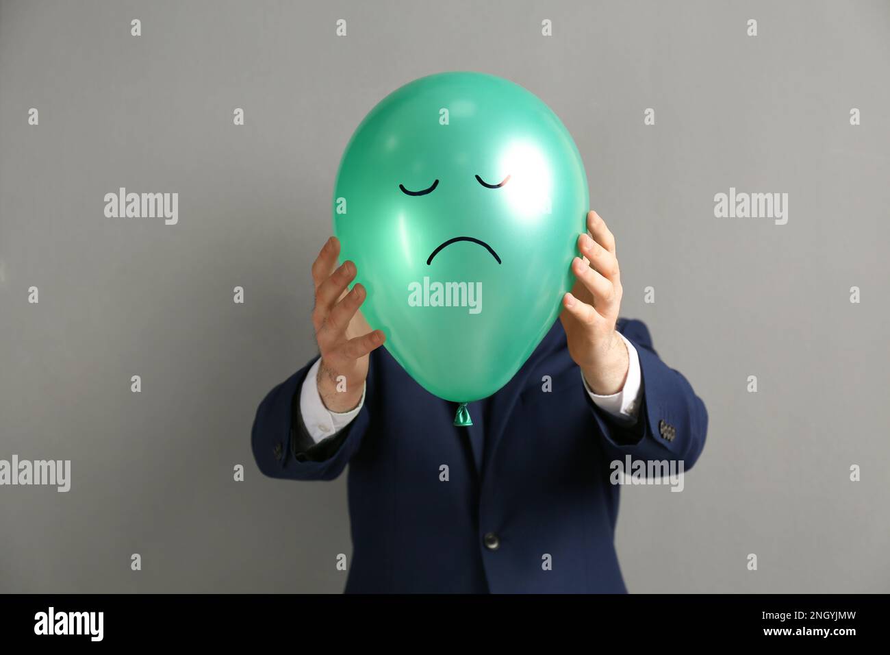 Man holding green air balloon with drawn sad face on grey background ...