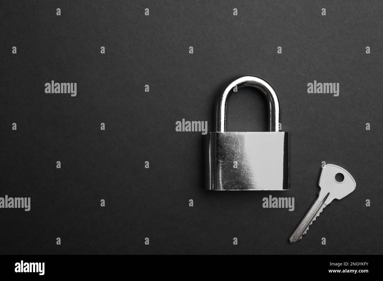 Modern padlock and key on black background, flat lay. Space for text ...