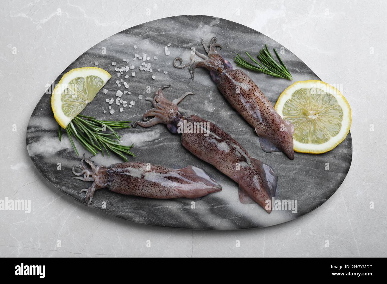 Fresh raw squids with lemon, rosemary and salt on light grey marble ...