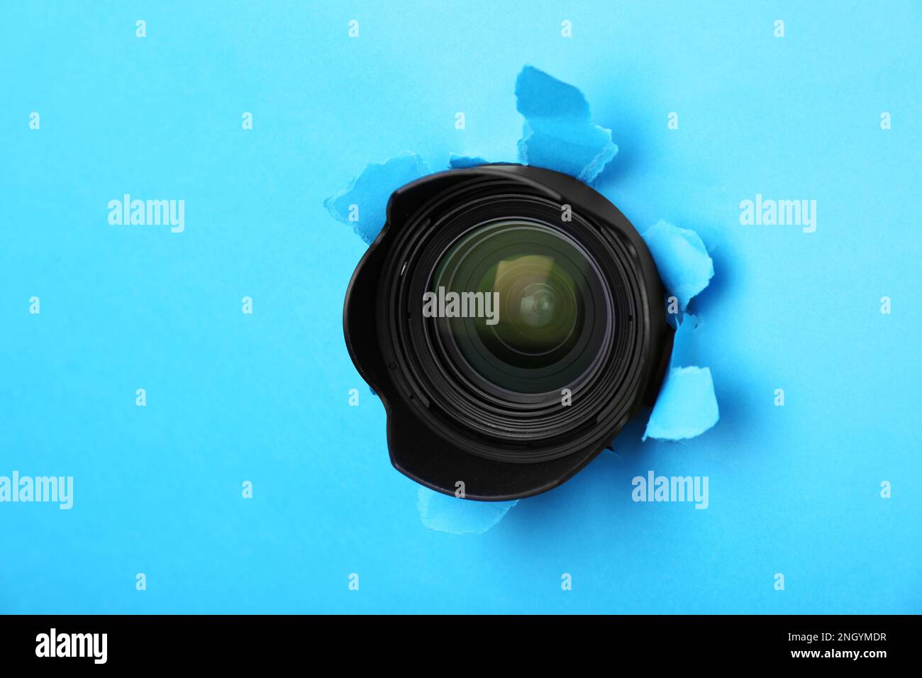 Hidden camera lens through torn hole in light blue paper Stock Photo ...