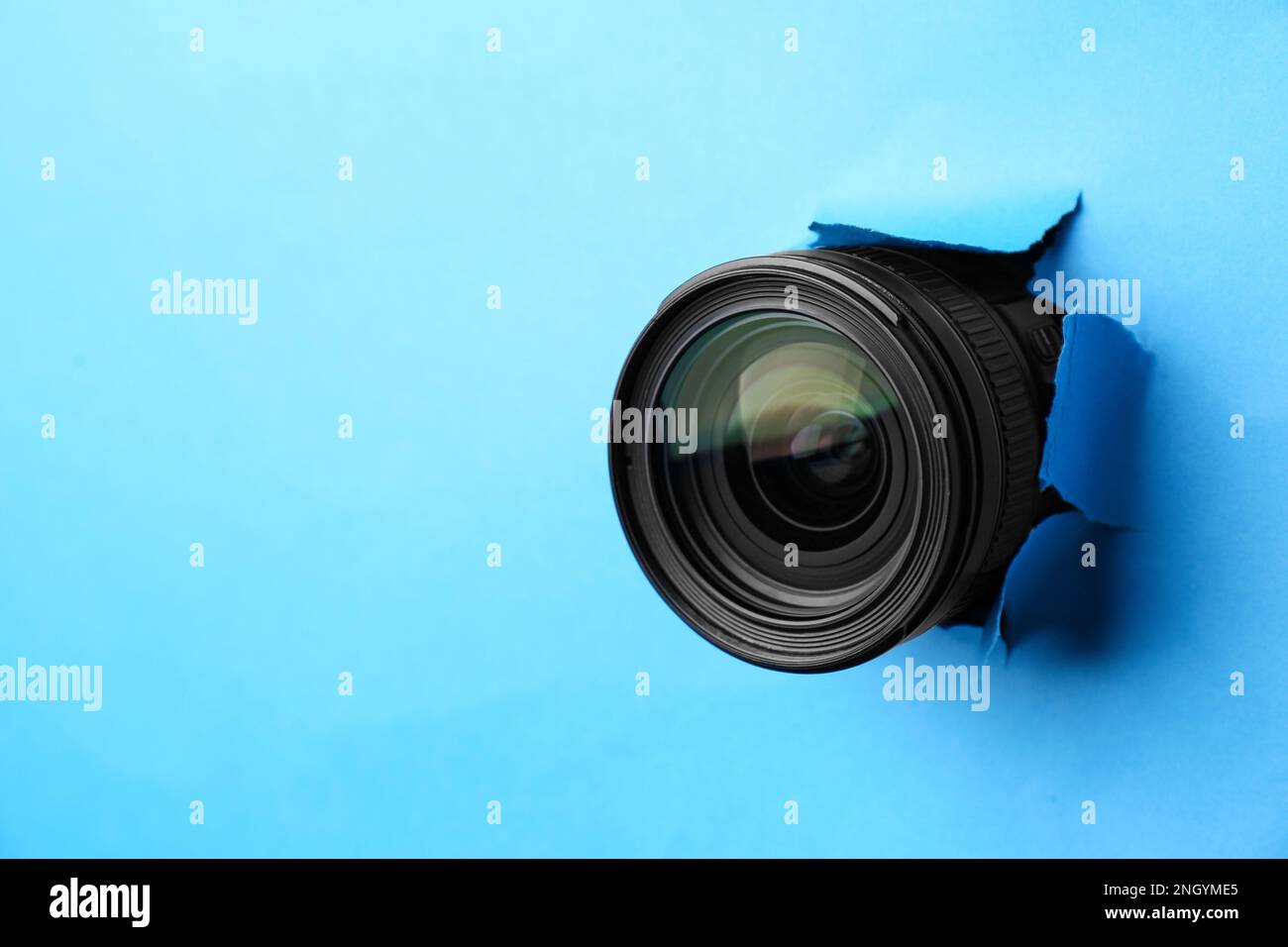 Hidden camera lens through torn hole in light blue paper. Space for ...