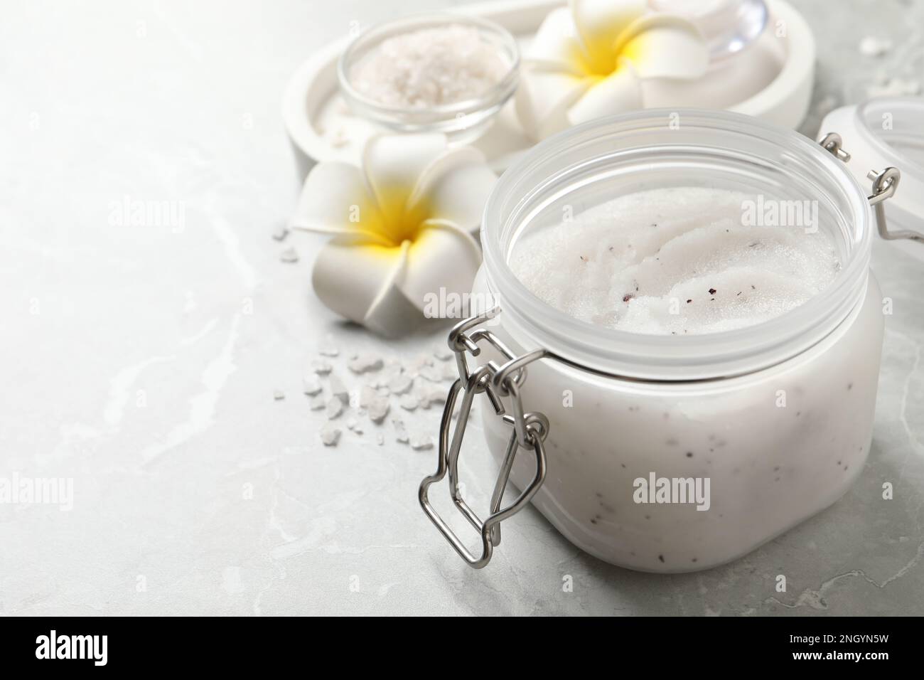 Body scrub in glass jar and plumeria flowers on grey marble table ...