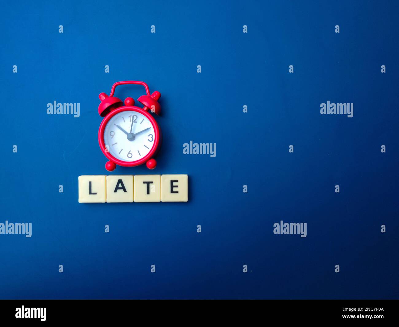 Red alarm clock with the word LATE on a blue background Stock Photo - Alamy