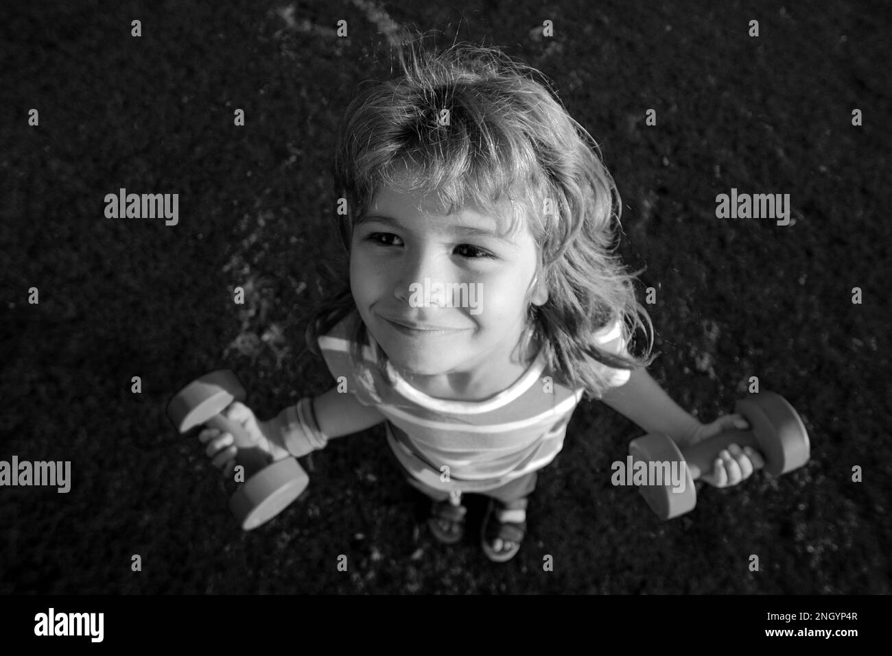 Strong little boy. Funny face of cute child with dumbbells. Children ...