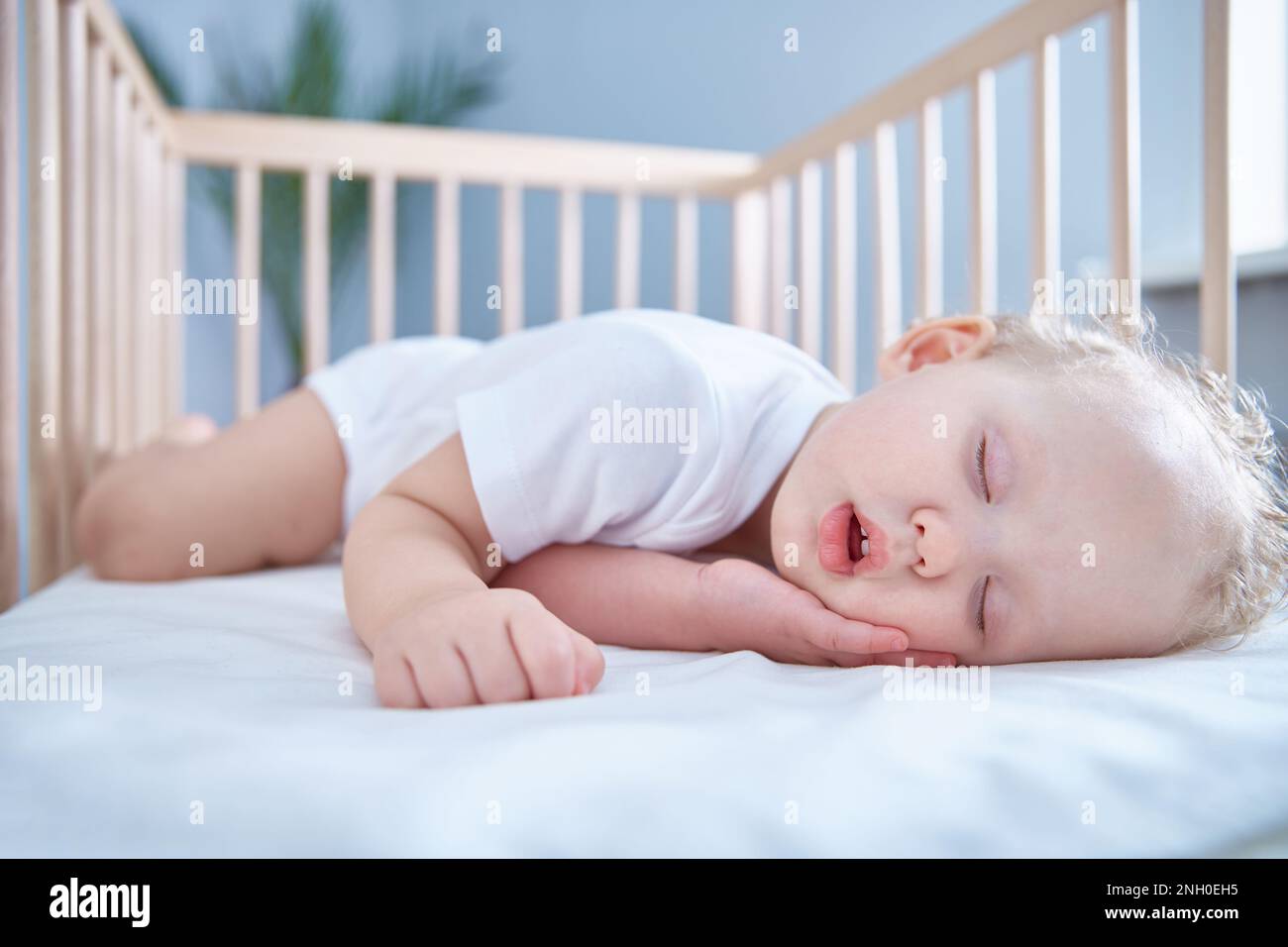 Baby sleeps in her baby wooden crib for newborns. A spacious, bright ...