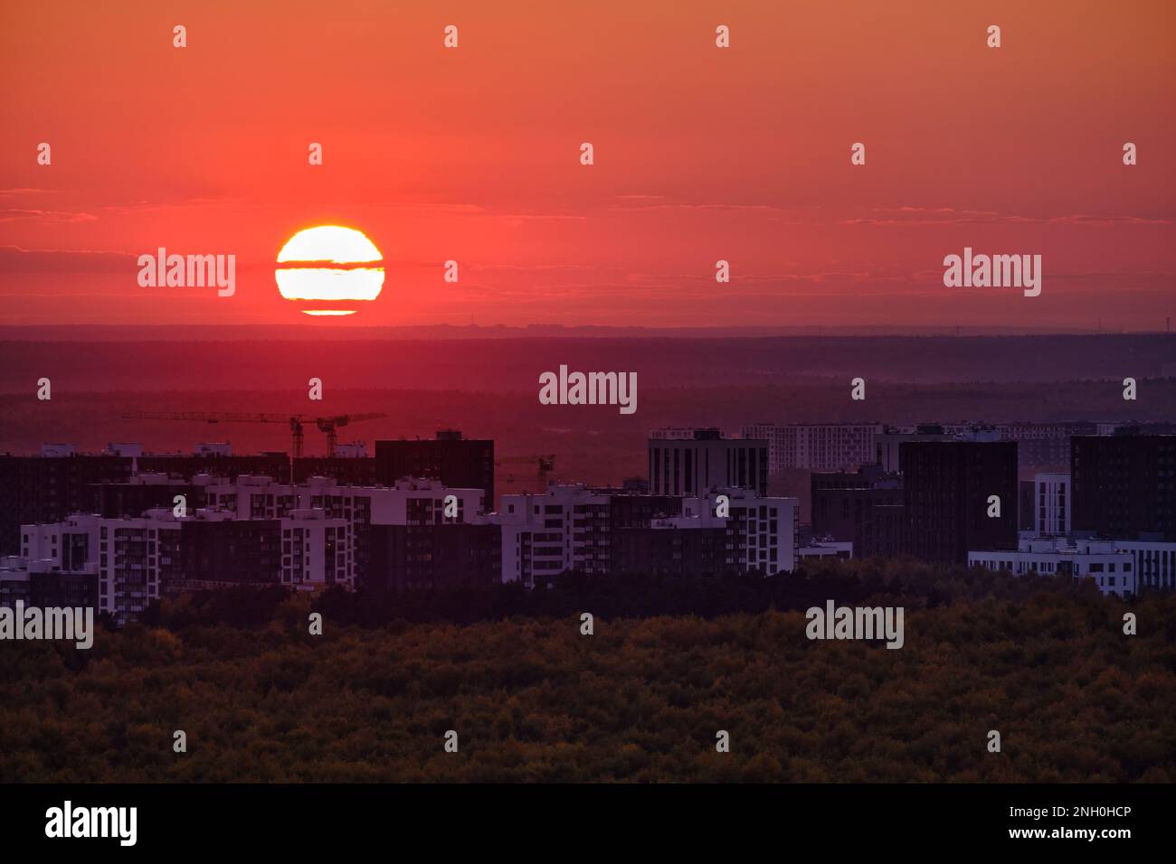 Big red sun over the roofs of city buildings, evening sunset. Cloudy ...