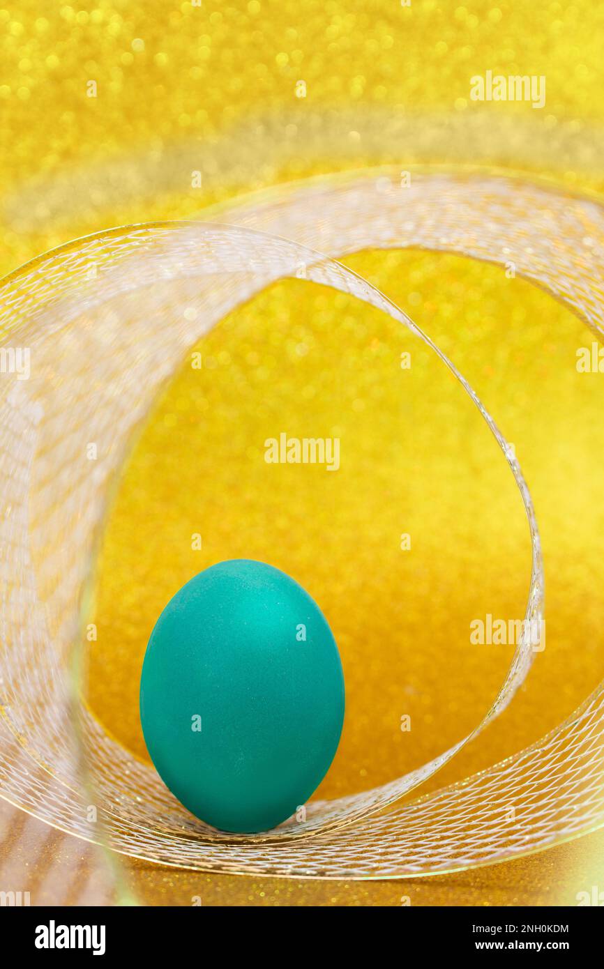 Blue egg stands on swirl mesh ribbon behind yellow shiny background ...