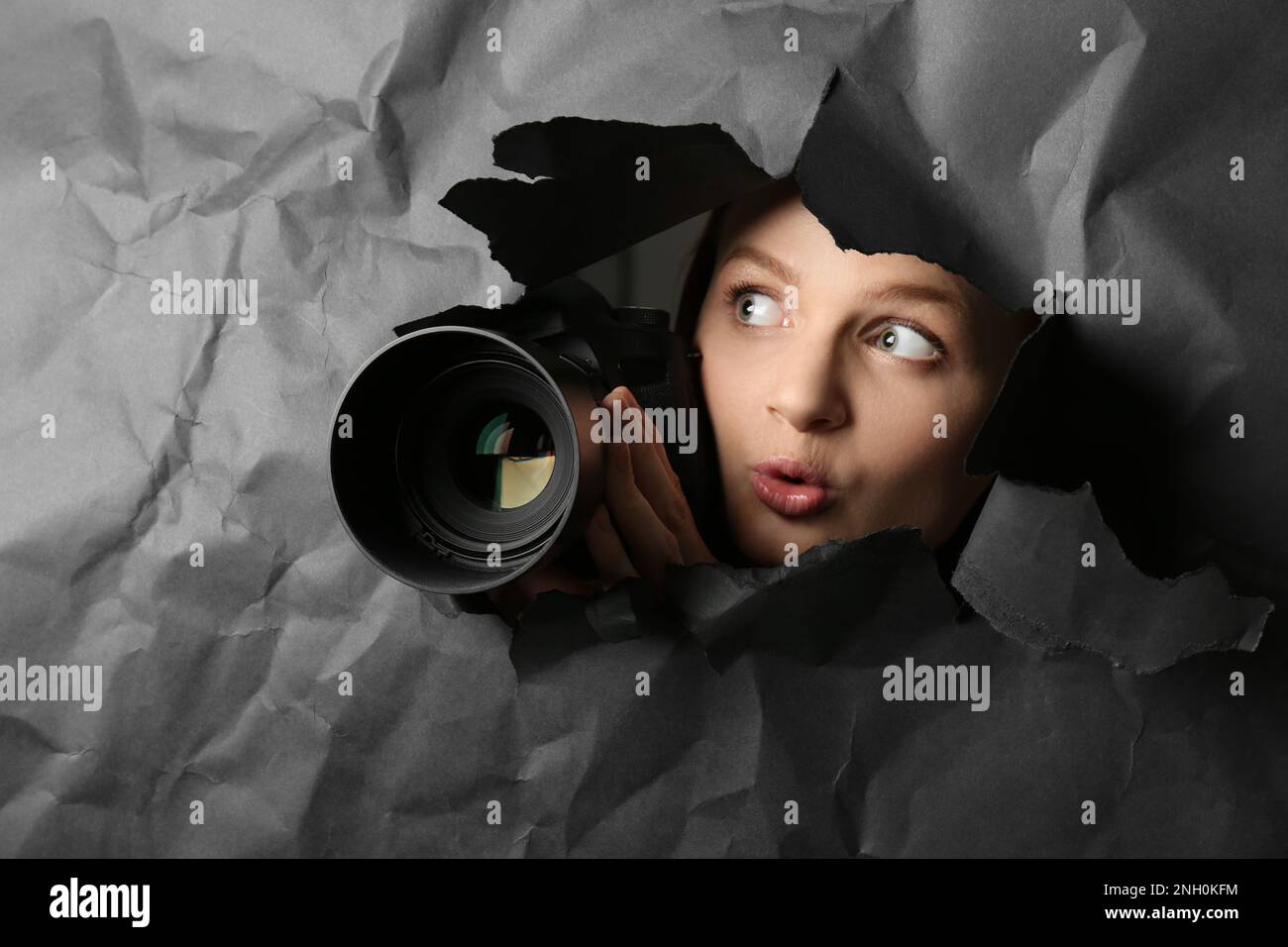 Hidden woman with camera spying through hole in black paper Stock Photo ...