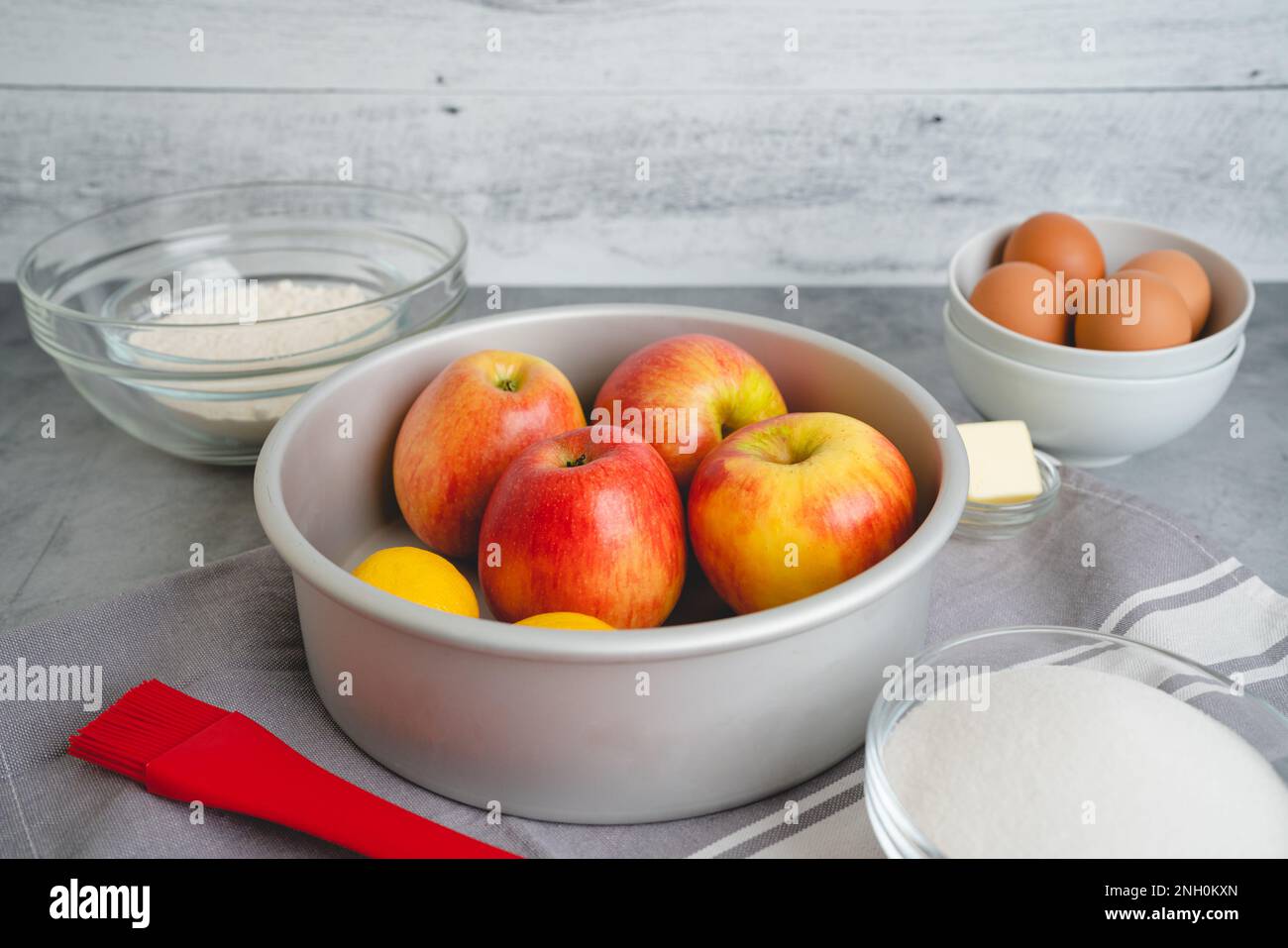 Baking pan, apples, lemons, eggs, sugar, and flour in bowls close-up on ...