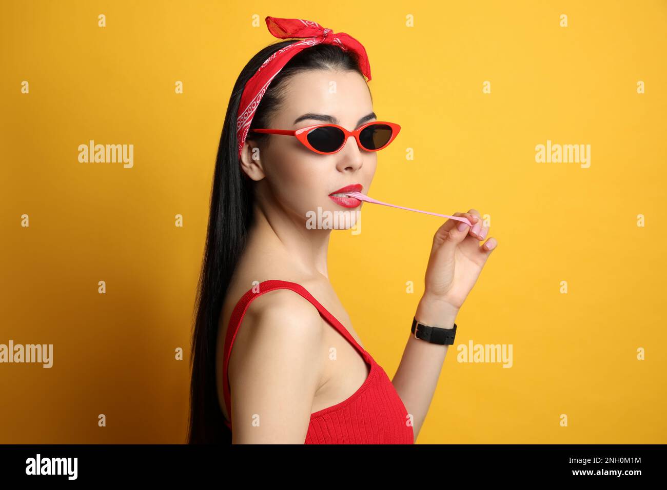 Fashionable young woman in pin up outfit chewing bubblegum on yellow ...