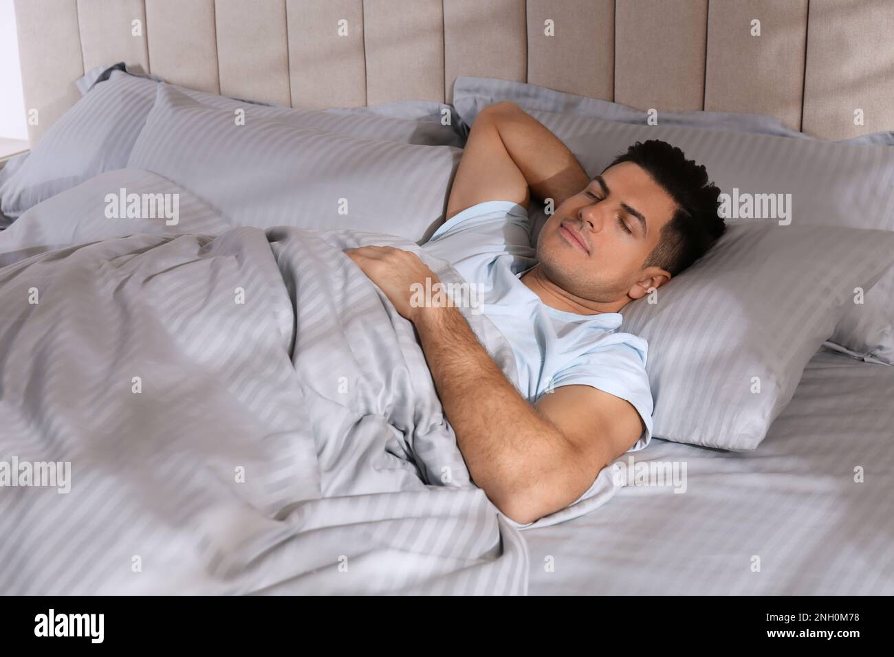 Man sleeping in comfortable bed with light grey striped linens Stock ...