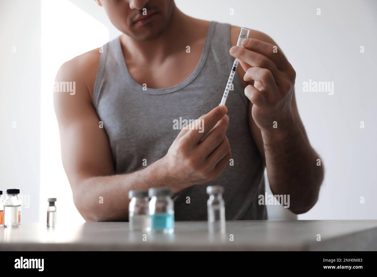 Athletic man filling syringe at table indoors, closeup. Doping concept ...