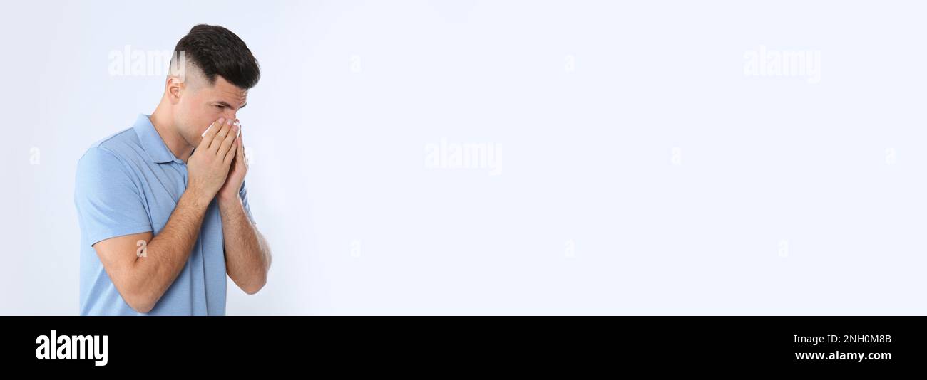 Man with tissue suffering from runny nose on white background Stock ...
