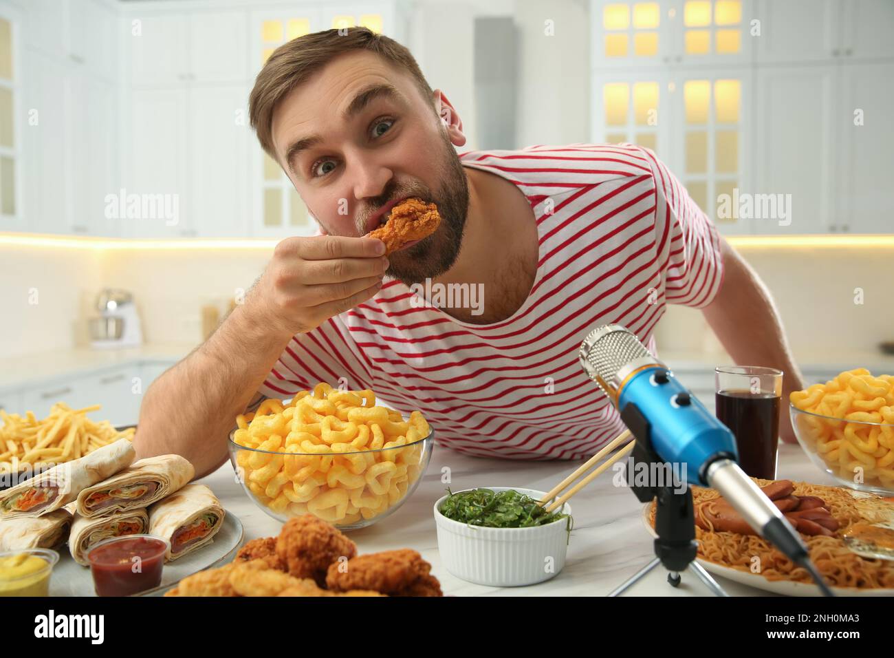 Food blogger eating near microphone at table in kitchen. Mukbang vlog ...