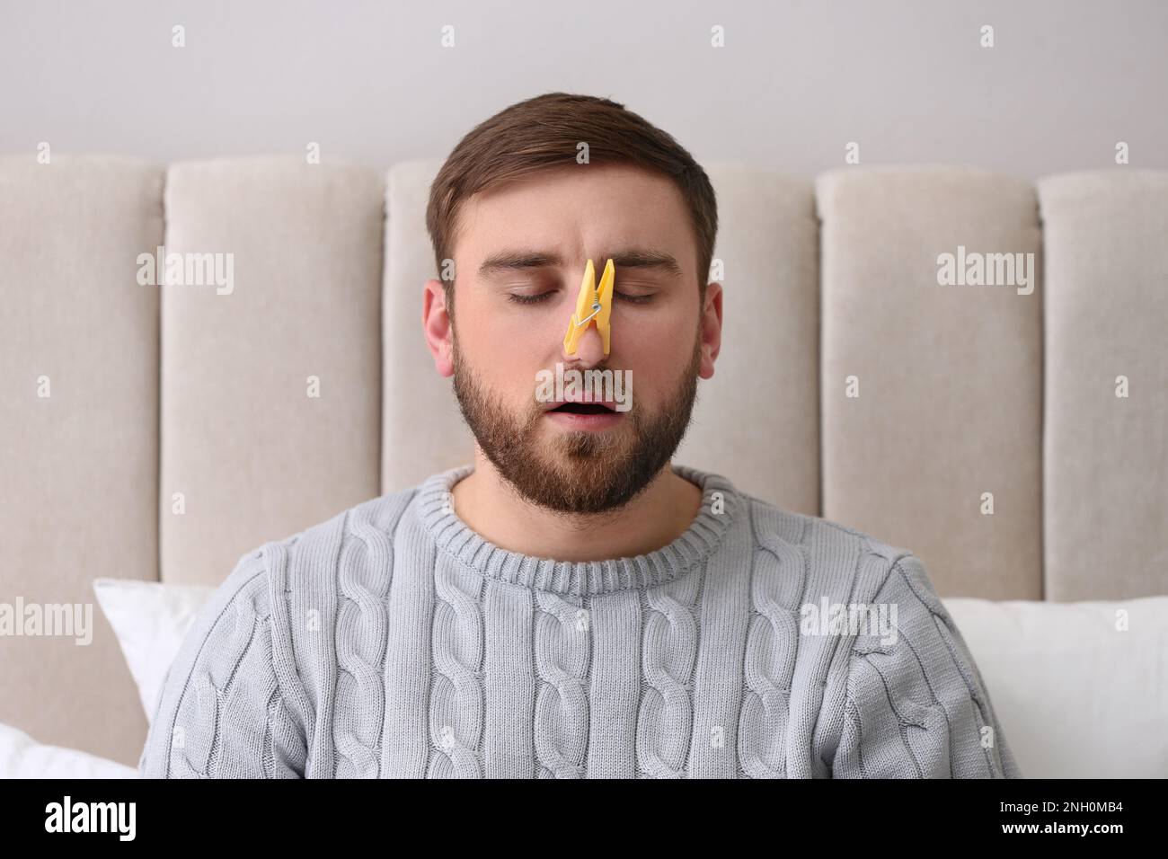 Young man with clothespin suffering from runny nose in bed indoors ...