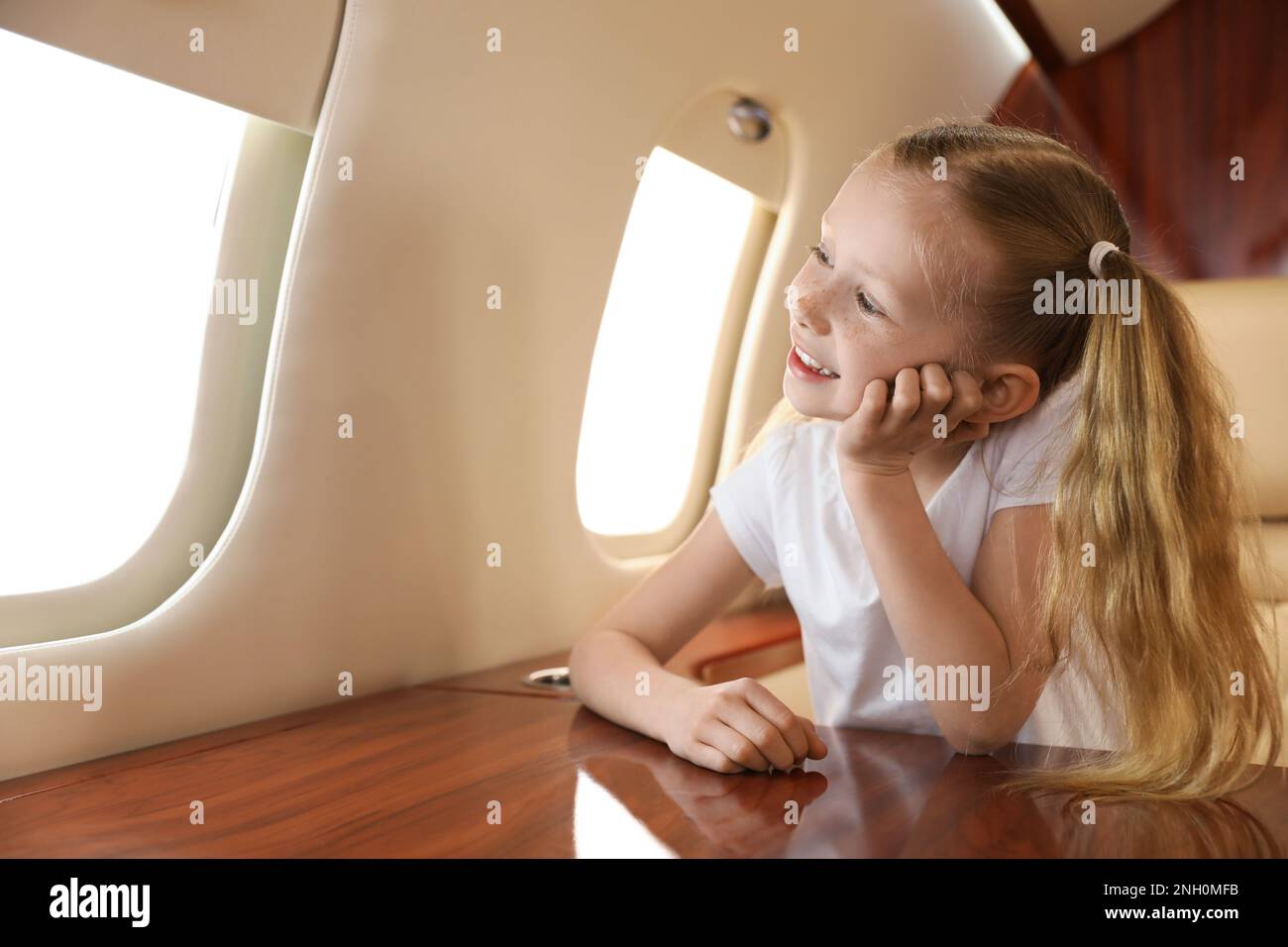 Cute little girl looking out window at table in airplane during flight ...
