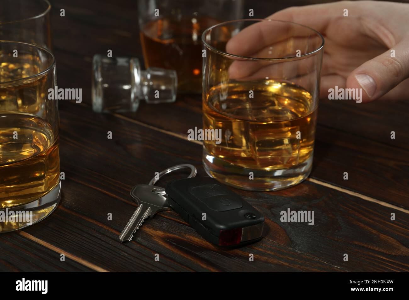 Man holding glass of alcohol near car key at wooden table, closeup ...