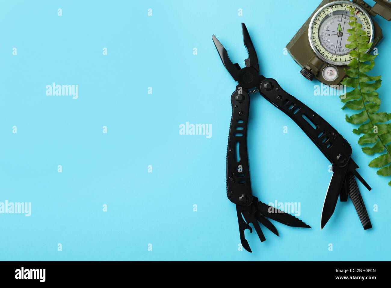 Compact portable multitool, compass and green leaf on light blue ...