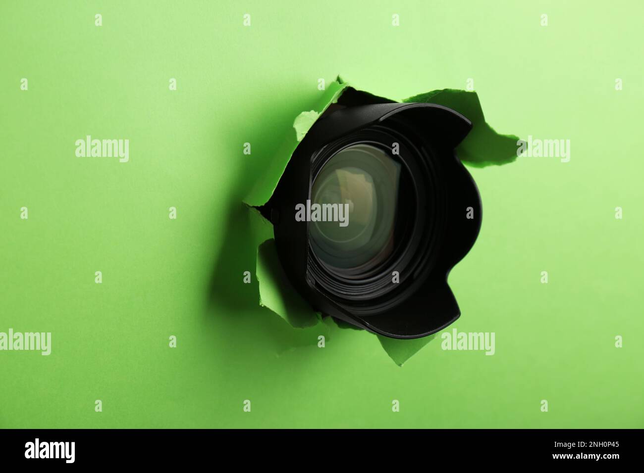 Hidden camera lens through torn hole in green paper Stock Photo - Alamy