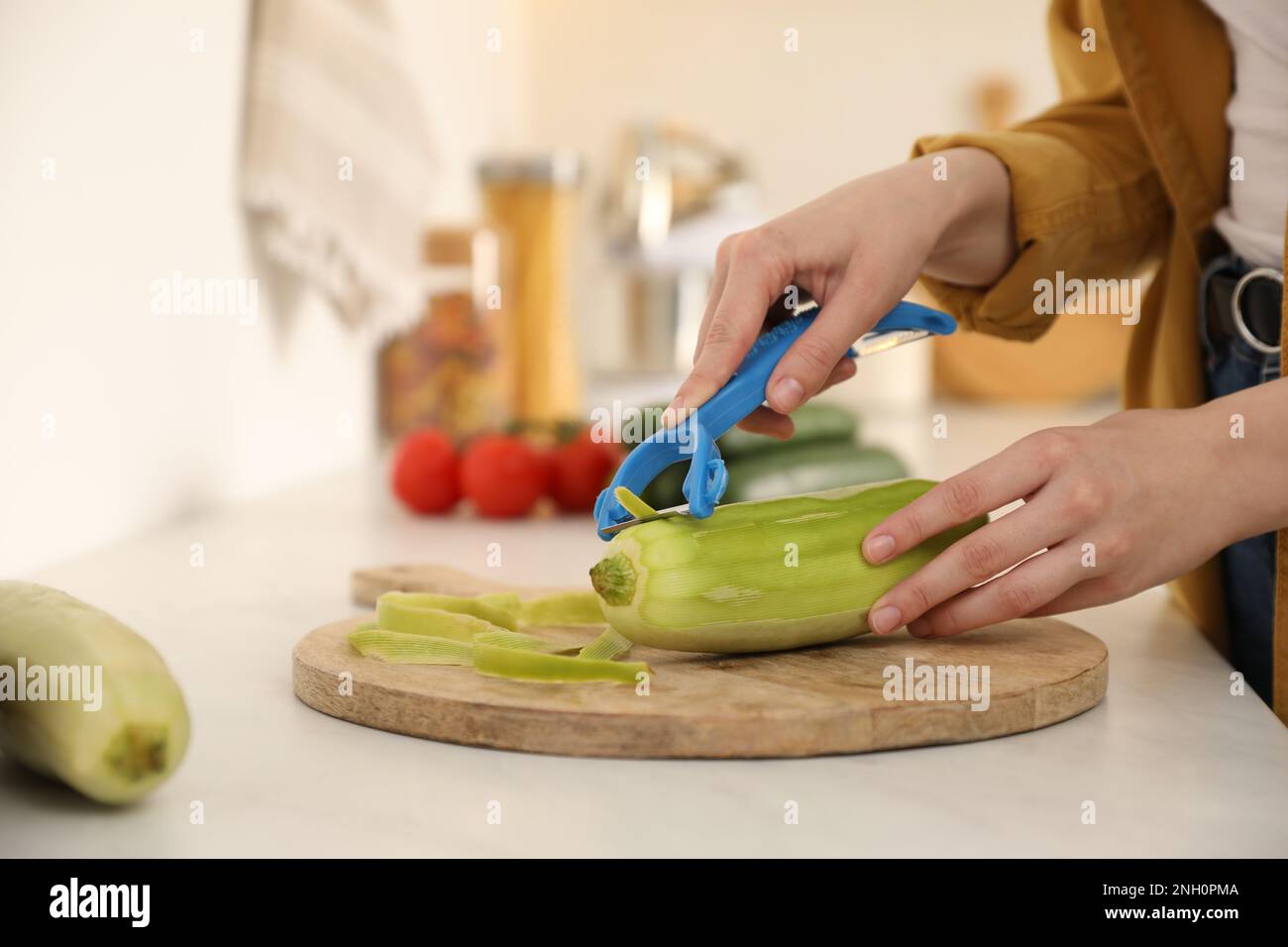 Woman peeling zucchini at kitchen counter, closeup. Preparing vegetable ...