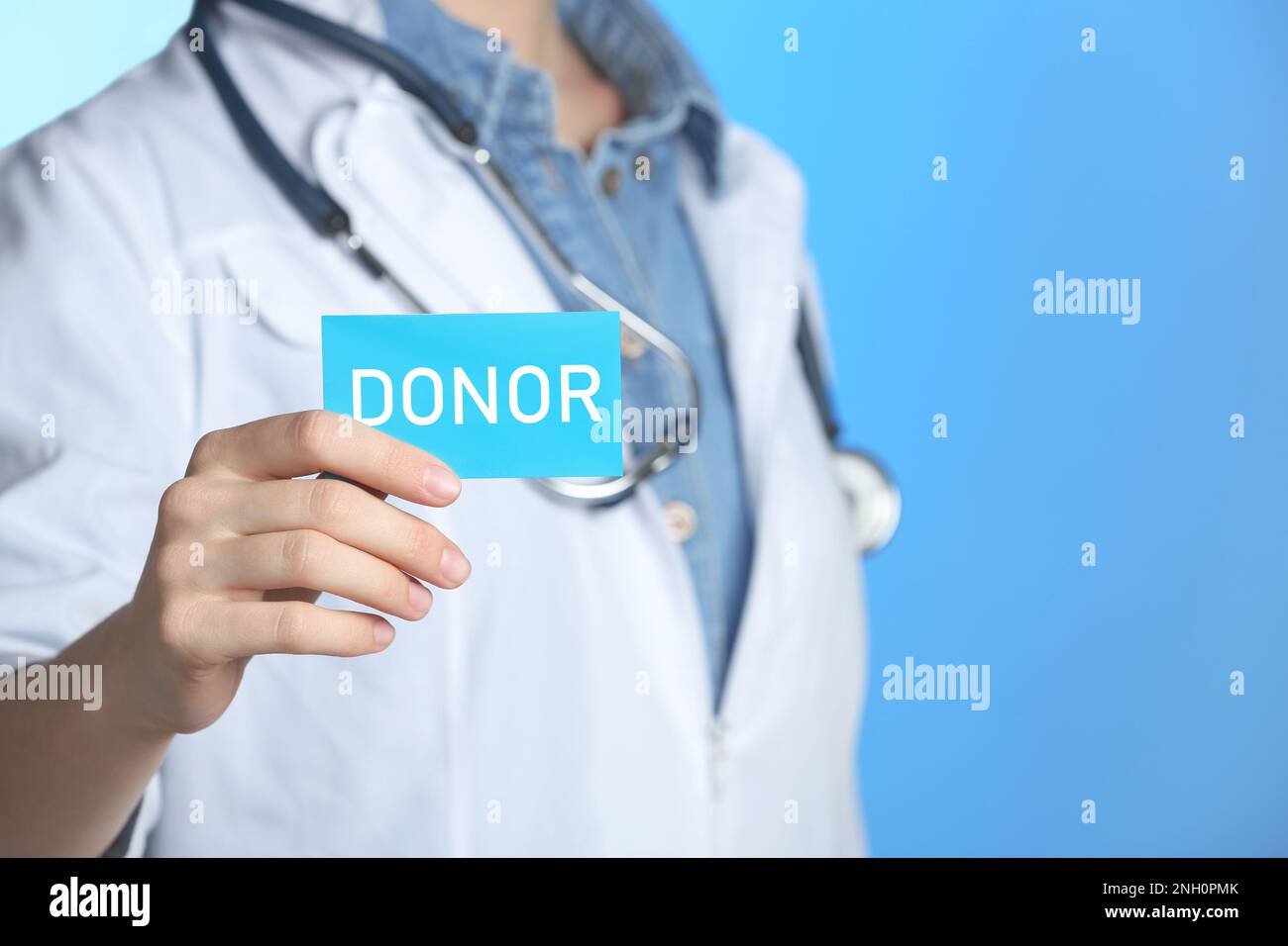 Doctor holding card with word DONOR on light blue background, closeup ...