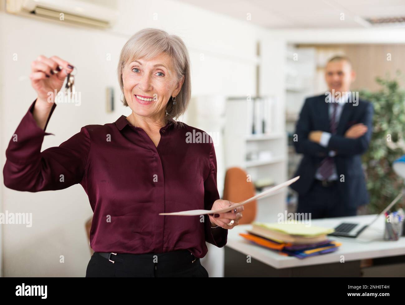 Happy elderly woman holding keys in real estate agent office Stock ...