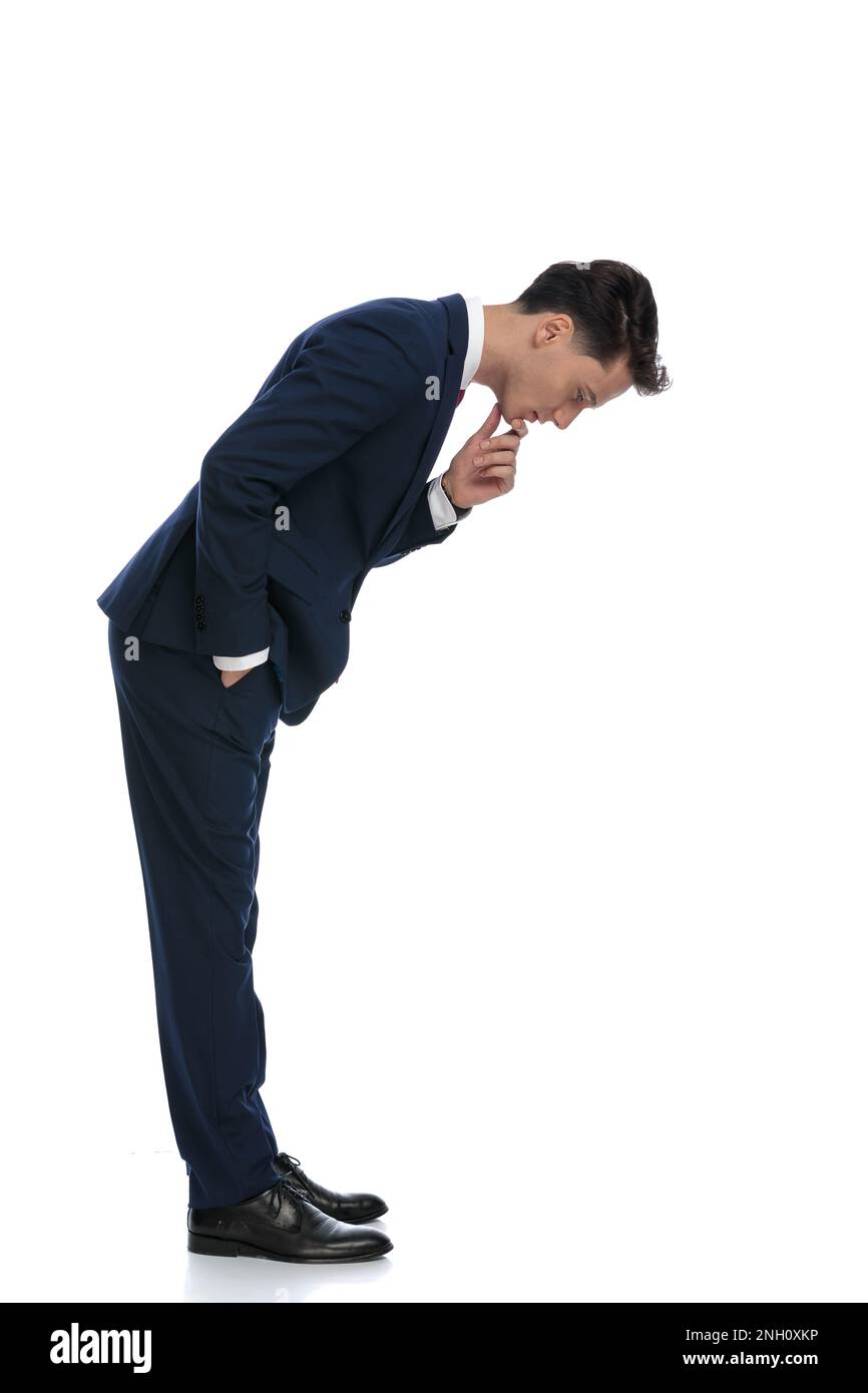 young businessman looking down and scratching his chin, wearing a suit ...
