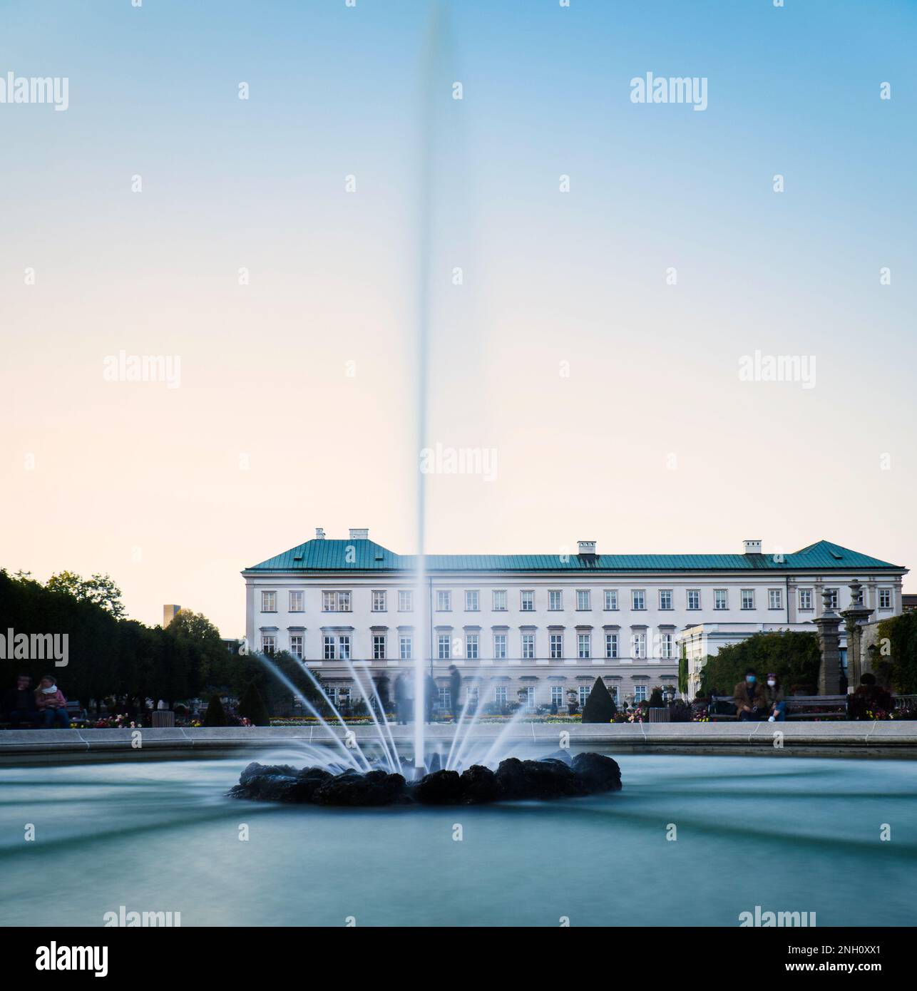 A majestic building towers behind a fountain, with clear water spraying ...