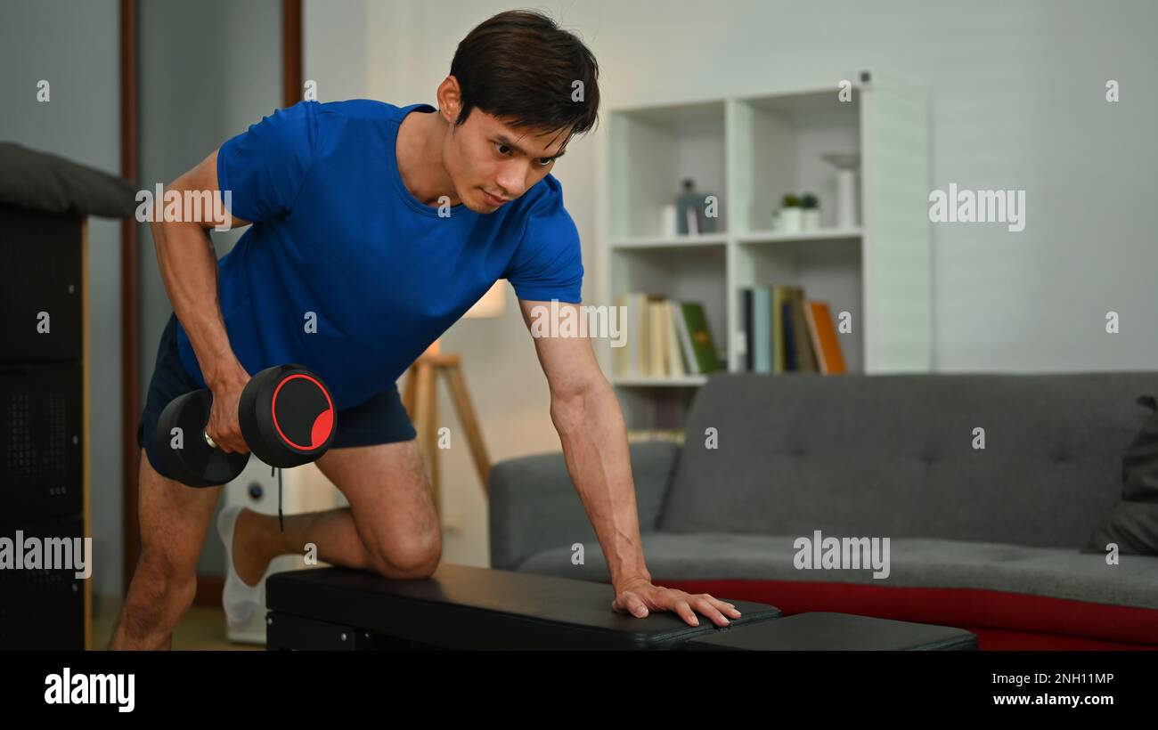 Athlete man doing exercise with dumbbell leaning on sports bench in ...