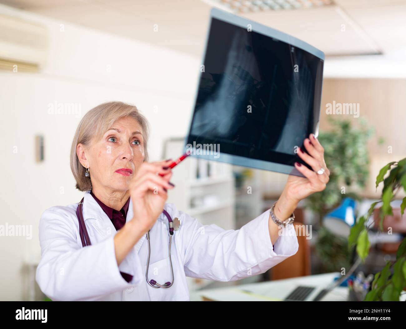 Aged female traumatologist looking at x-ray of foot in clinic office ...