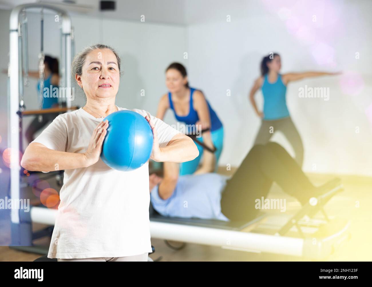 Positive old female squeezing ball in hands during Pilates training in ...