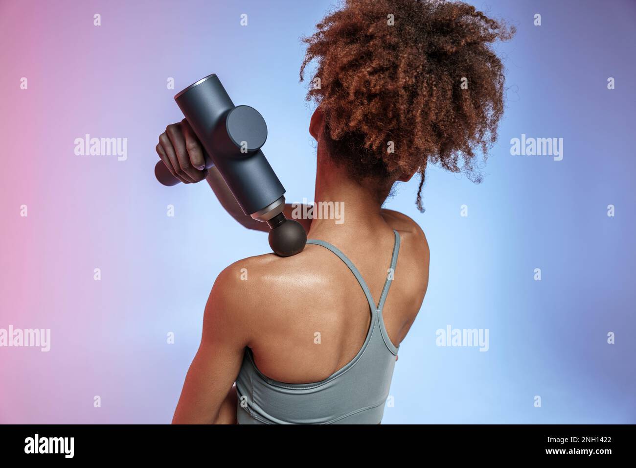 Back view of woman use massage gun machine rehab after muscle workout standing on studio ...