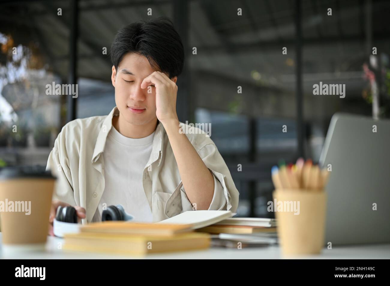 Unhappy and upset young Asian male college student sits at the coffee ...