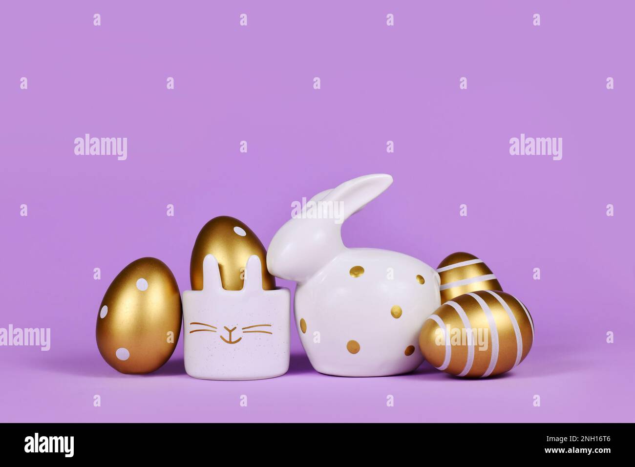 Easter decoration with easter bunny, golden eggs and egg cup on violet ...
