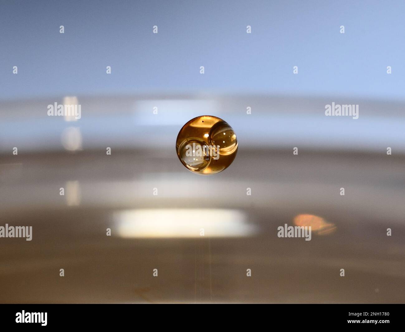 A crystal clear drop of water suspended in a shallow bowl of reflective ...
