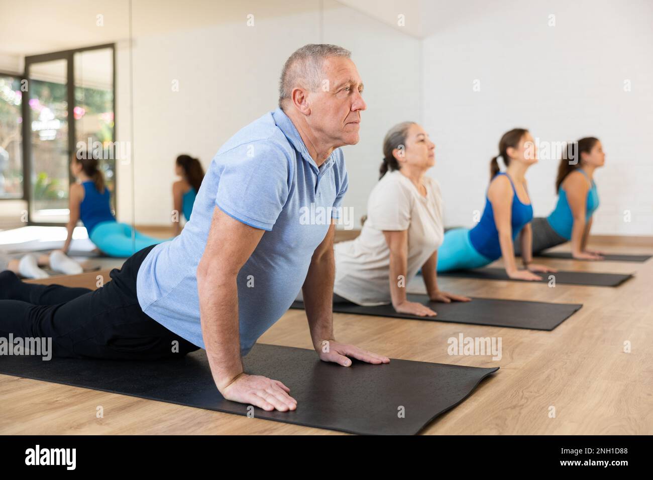 Class of male and women of different ages in active wear doing cobra ...