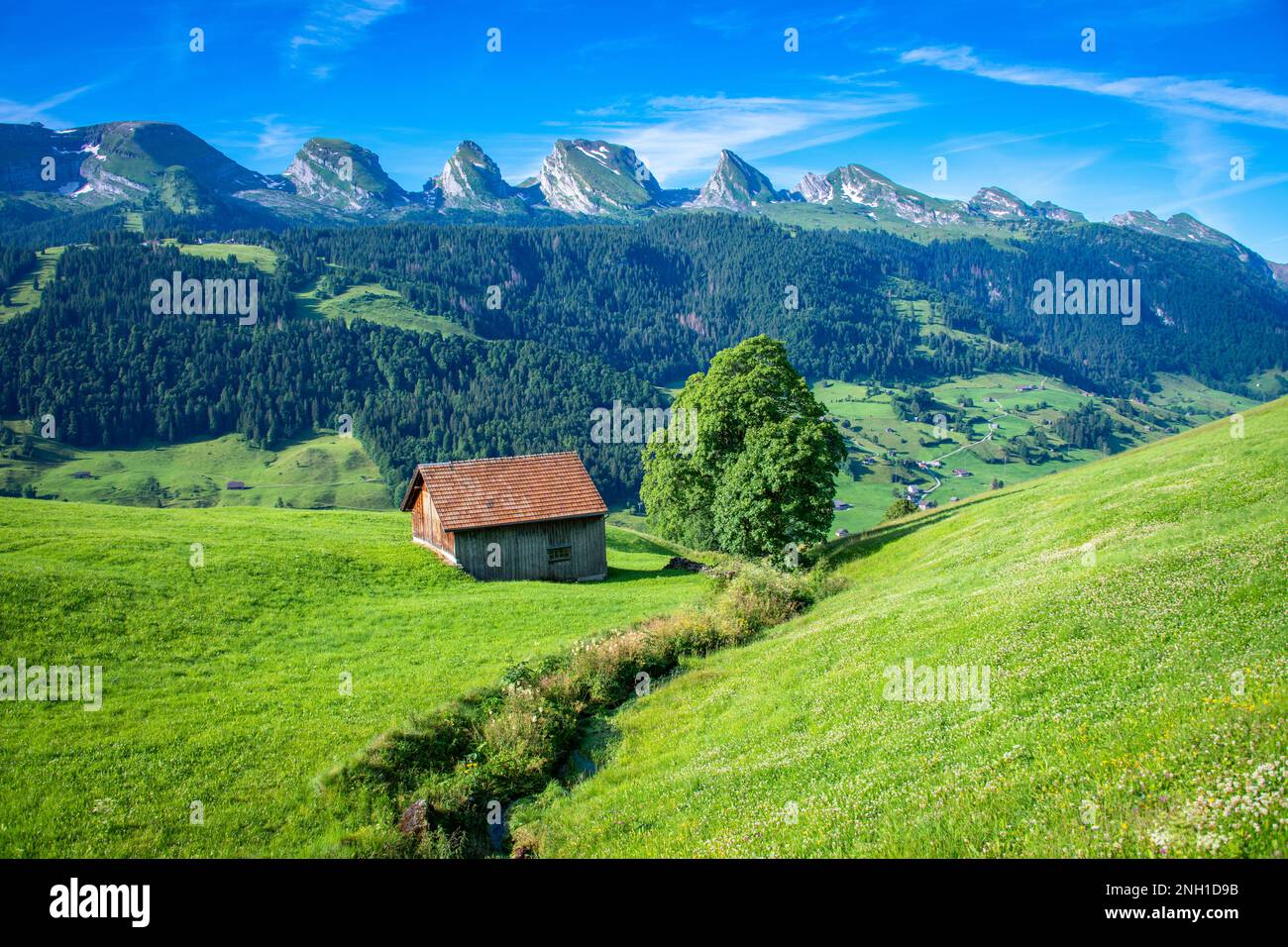 A hut standing in the valley surrounded by mountains under a blue sky ...