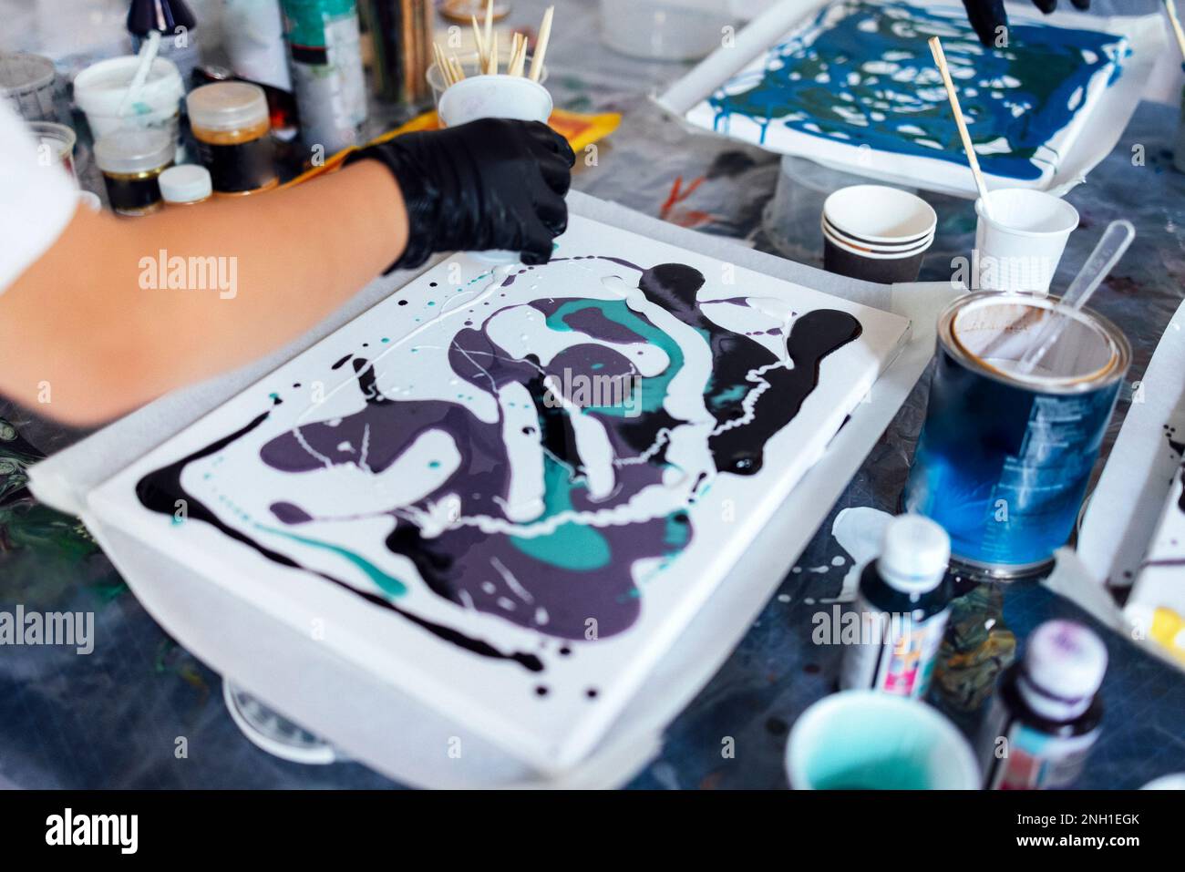 Master class on an Acrylic Fluid Pouring. Teacher and teen girl paint with liquid acrylic in an ...