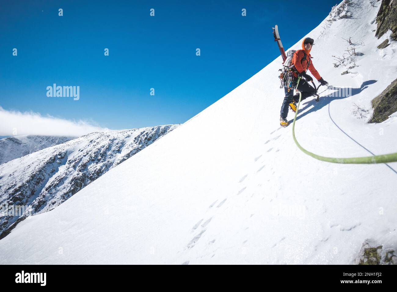 Man walking uphill with ice climbing tools and skis on his back Stock ...